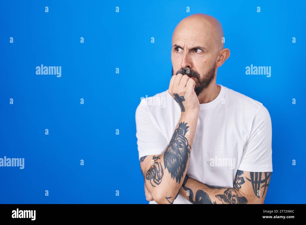 Hispanic man with tattoos standing over blue background looking ...