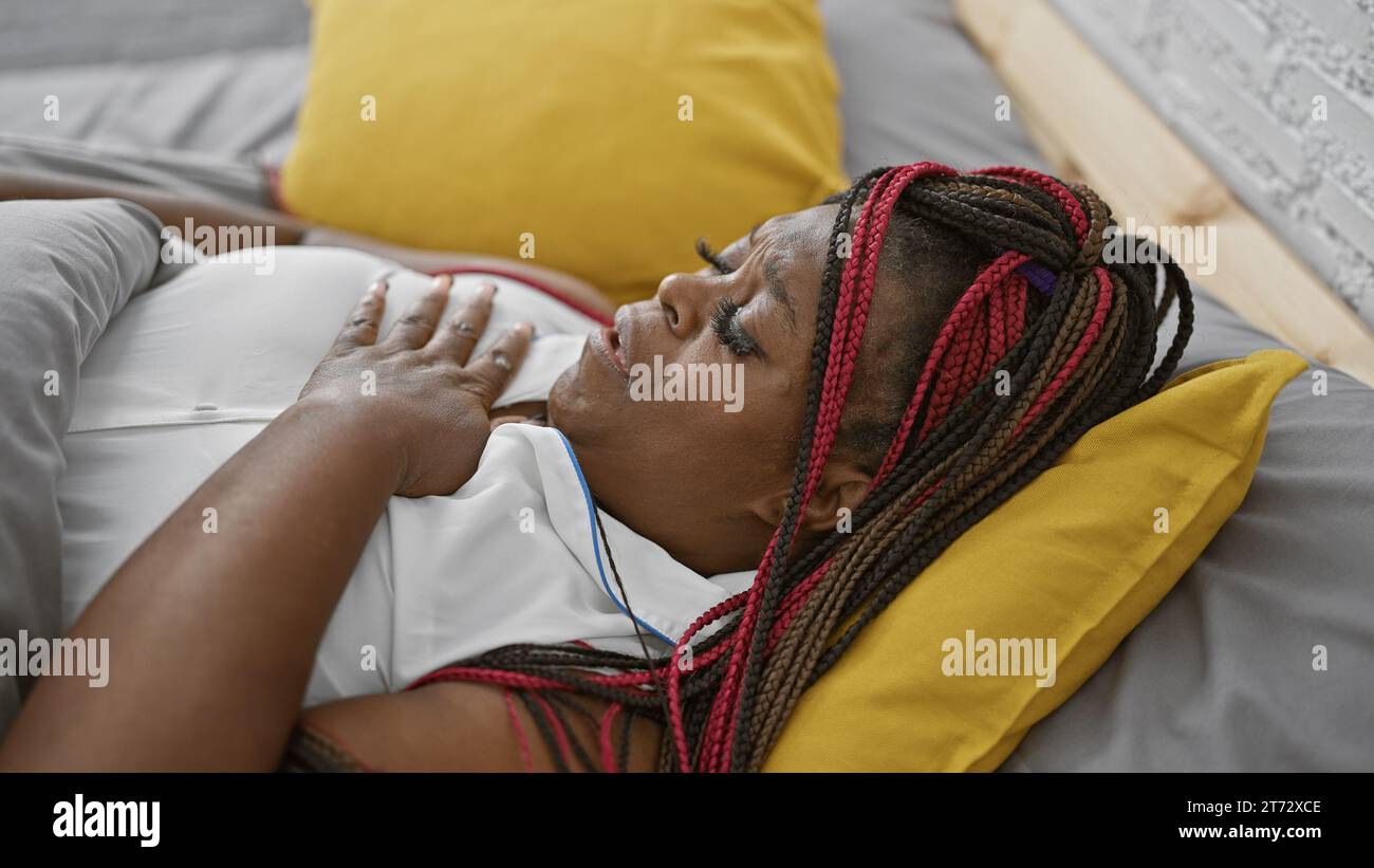 Exhausted african american woman in braids, comfortably lying on a cozy ...