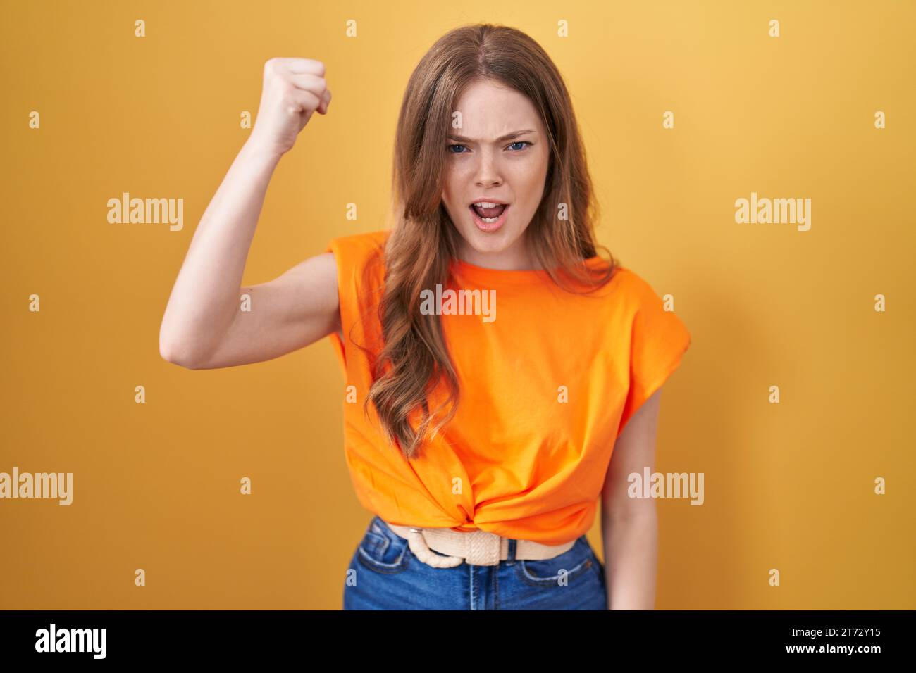 Caucasian woman standing over yellow background angry and mad raising ...