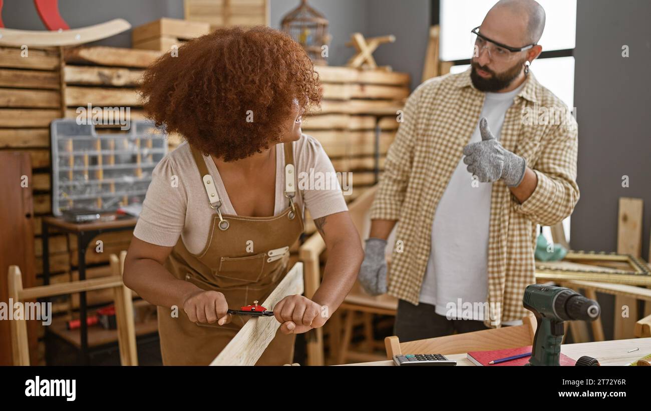 Two professional carpenters give a thumb up gesture while sanding a wood plank at their ...