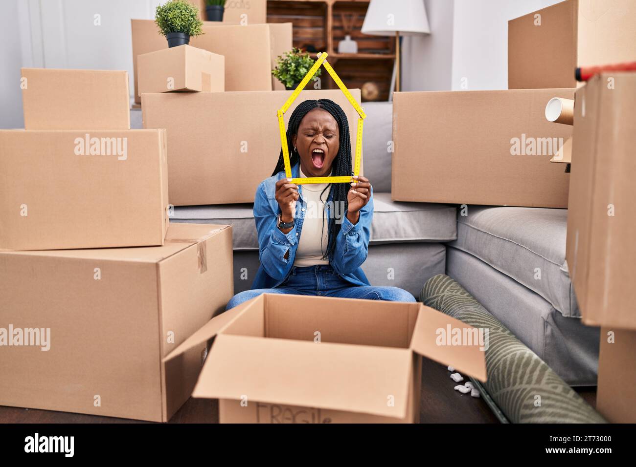 African woman with braids sitting on the floor at new home holding ...