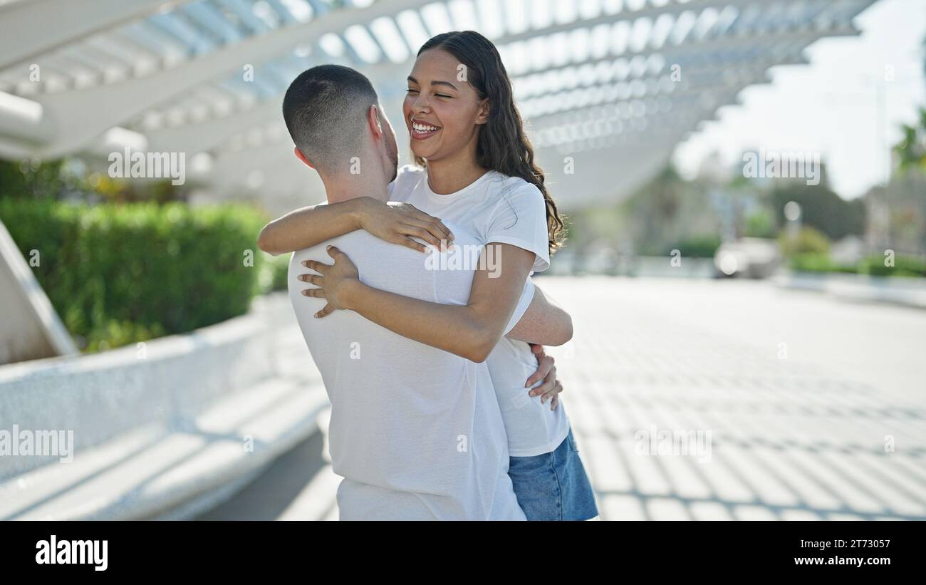 Confident, beautiful couple hugging and joyfully smiling in a sunny ...