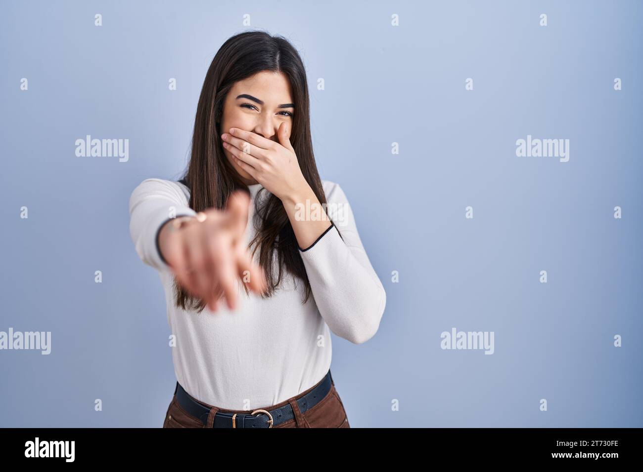 Young brunette woman standing over blue background laughing at you ...