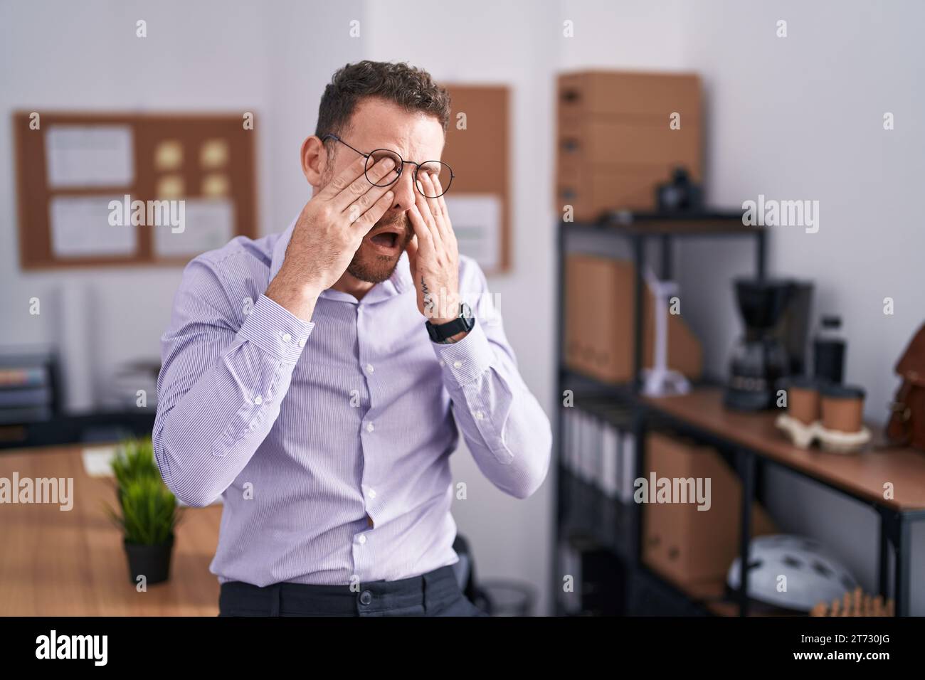 Young hispanic man at the office rubbing eyes for fatigue and headache ...