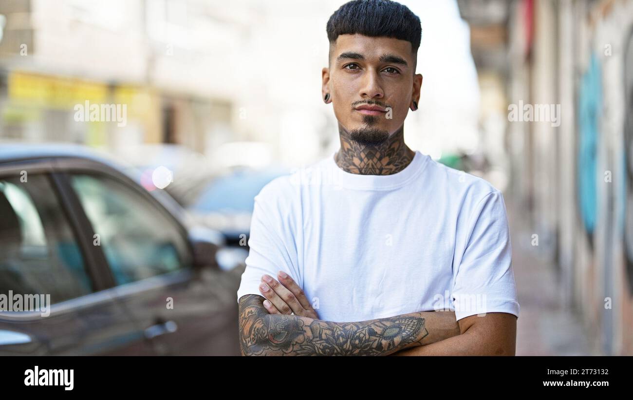 Cool young latin man with tattooed arms, standing outdoors on the urban ...