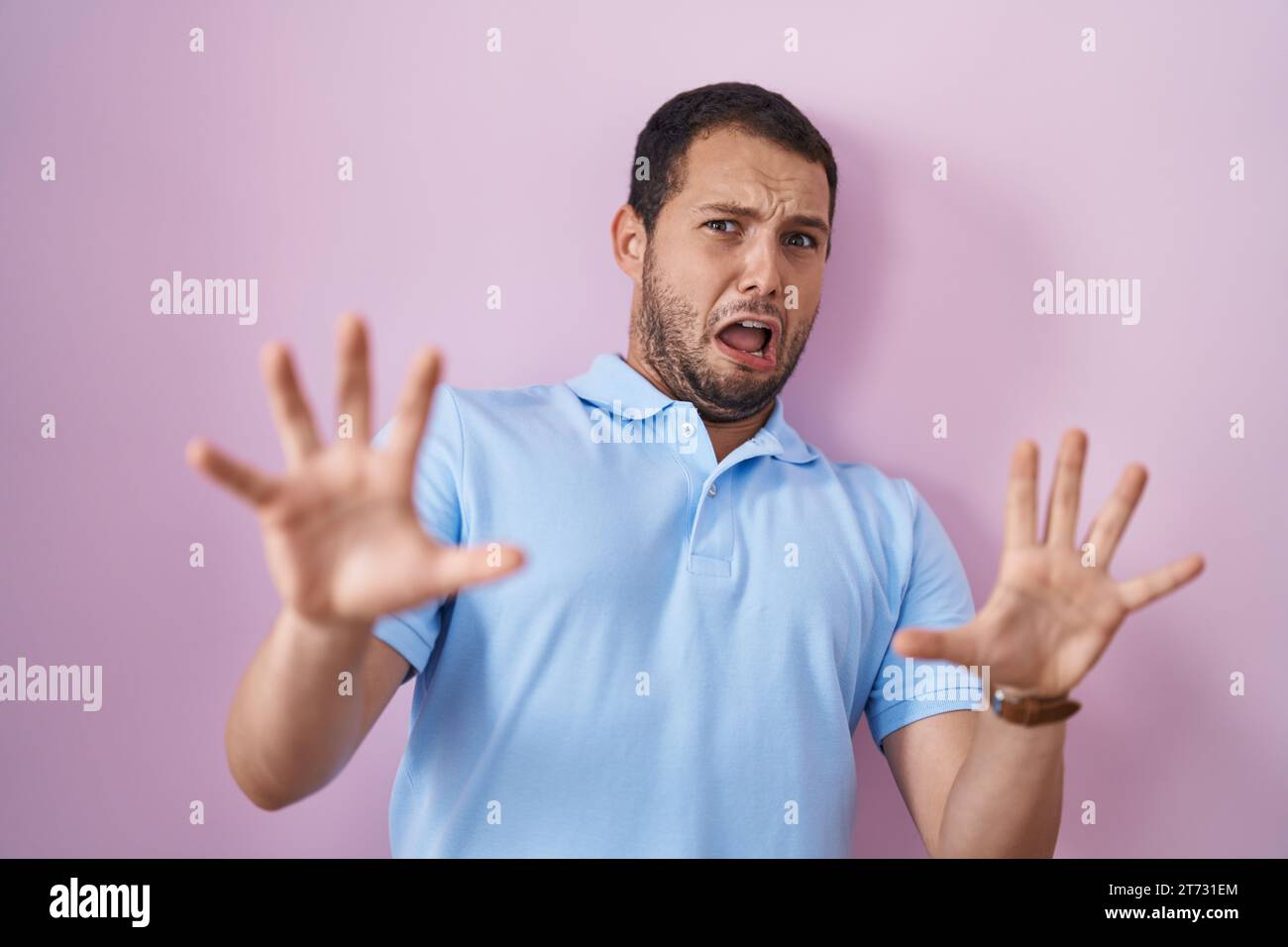 Hispanic man standing over pink background afraid and terrified with ...