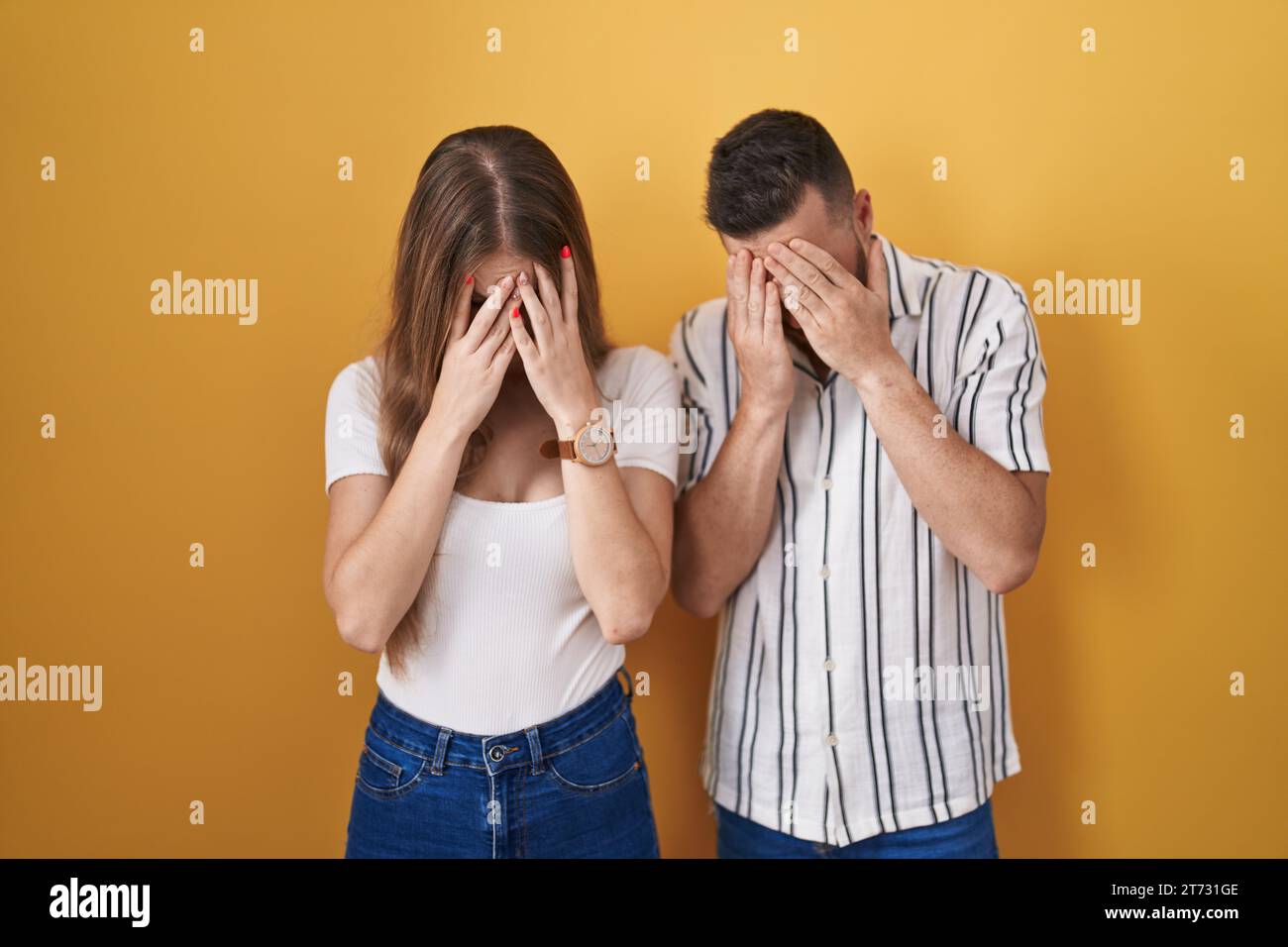 Young couple standing over yellow background with sad expression ...
