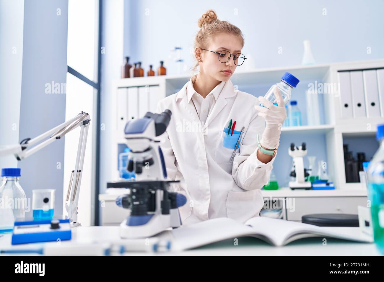 Young blonde woman scientist writing on notebook holding bottle at ...