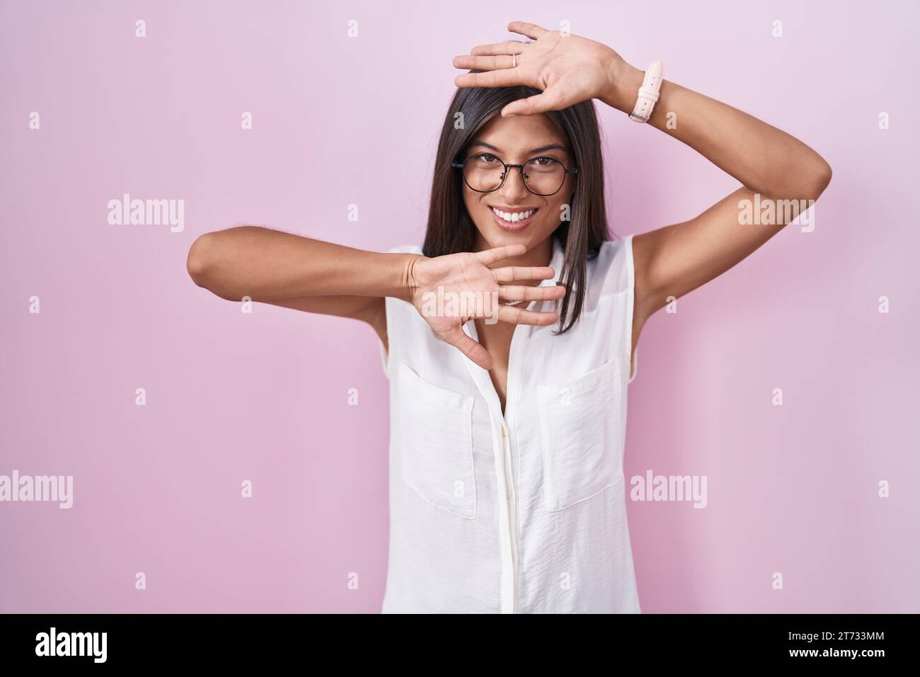 Brunette young woman standing over pink background wearing glasses ...