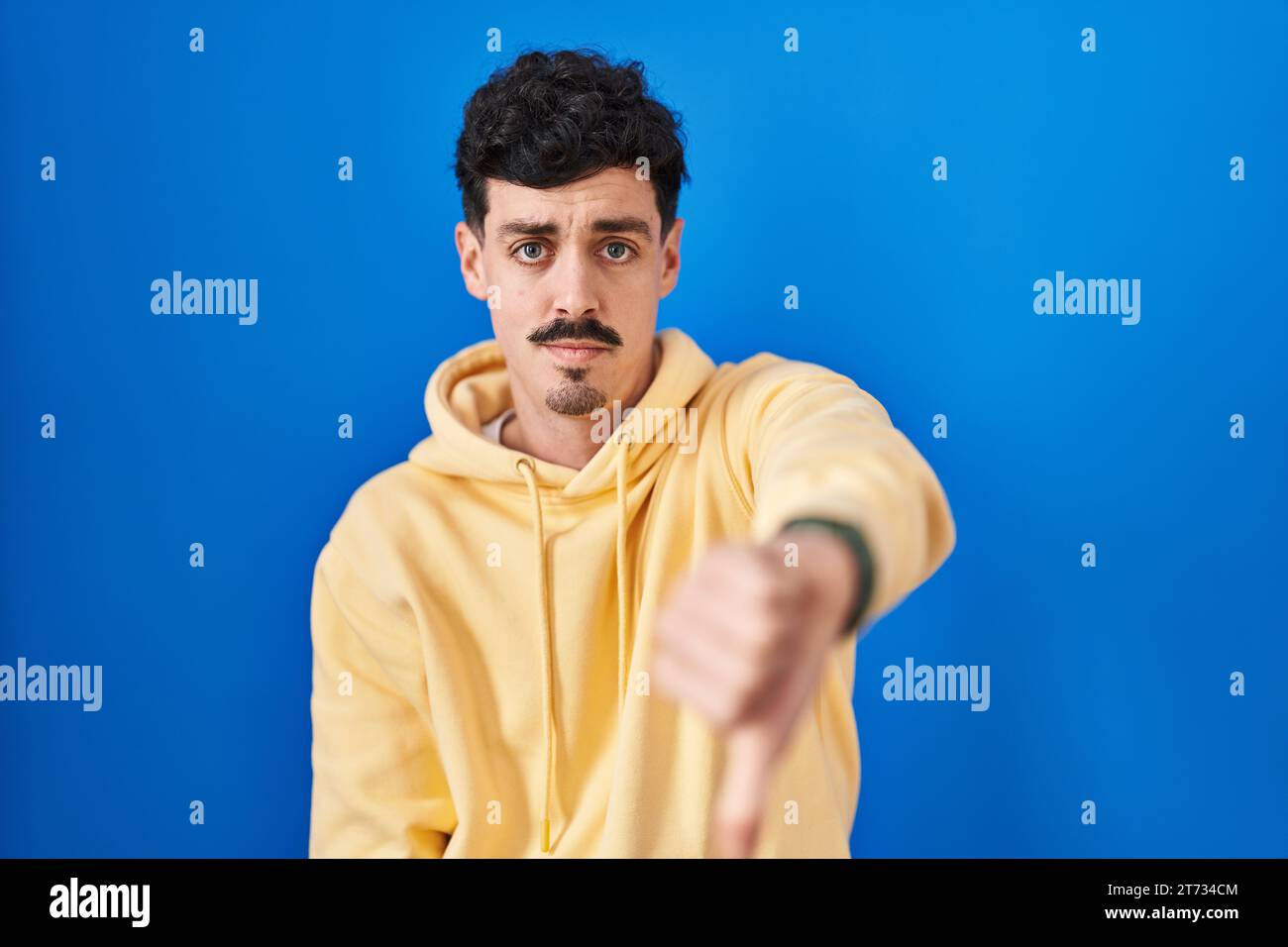 Hispanic man standing over blue background looking unhappy and angry ...