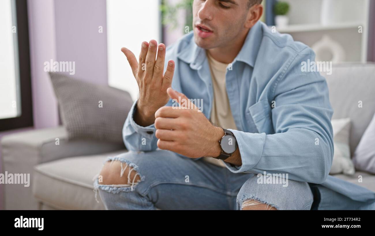 Unhappy, young hispanic man reluctantly sitting in his cozy living room ...