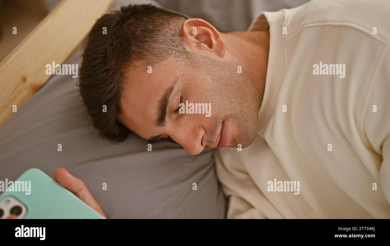 Exhausted young hispanic man, holding his phone, deeply asleep, resting comfortably in a cozy ...