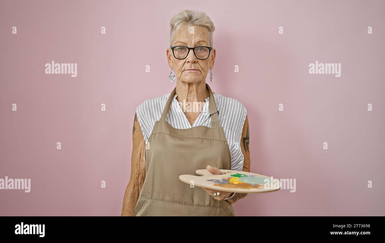Mature grey-haired woman artist, with brush and palette, painting with ...