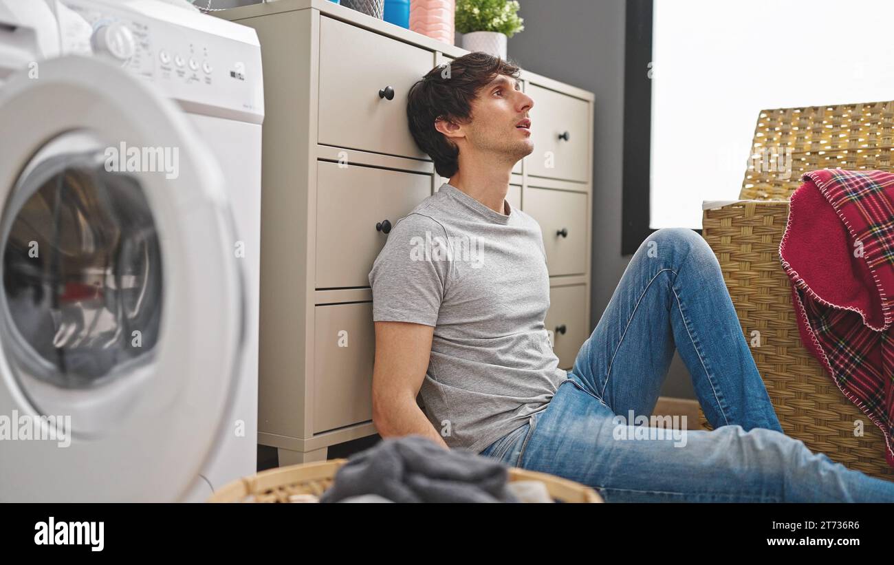 Young hispanic man waiting for washing machine with serious face at ...
