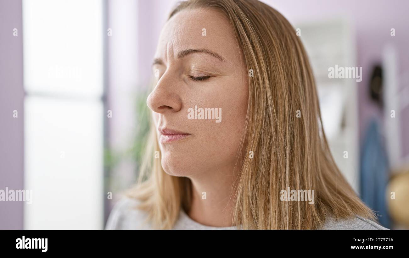 Stunning young blonde woman calmly takes a healing breath with her eyes ...