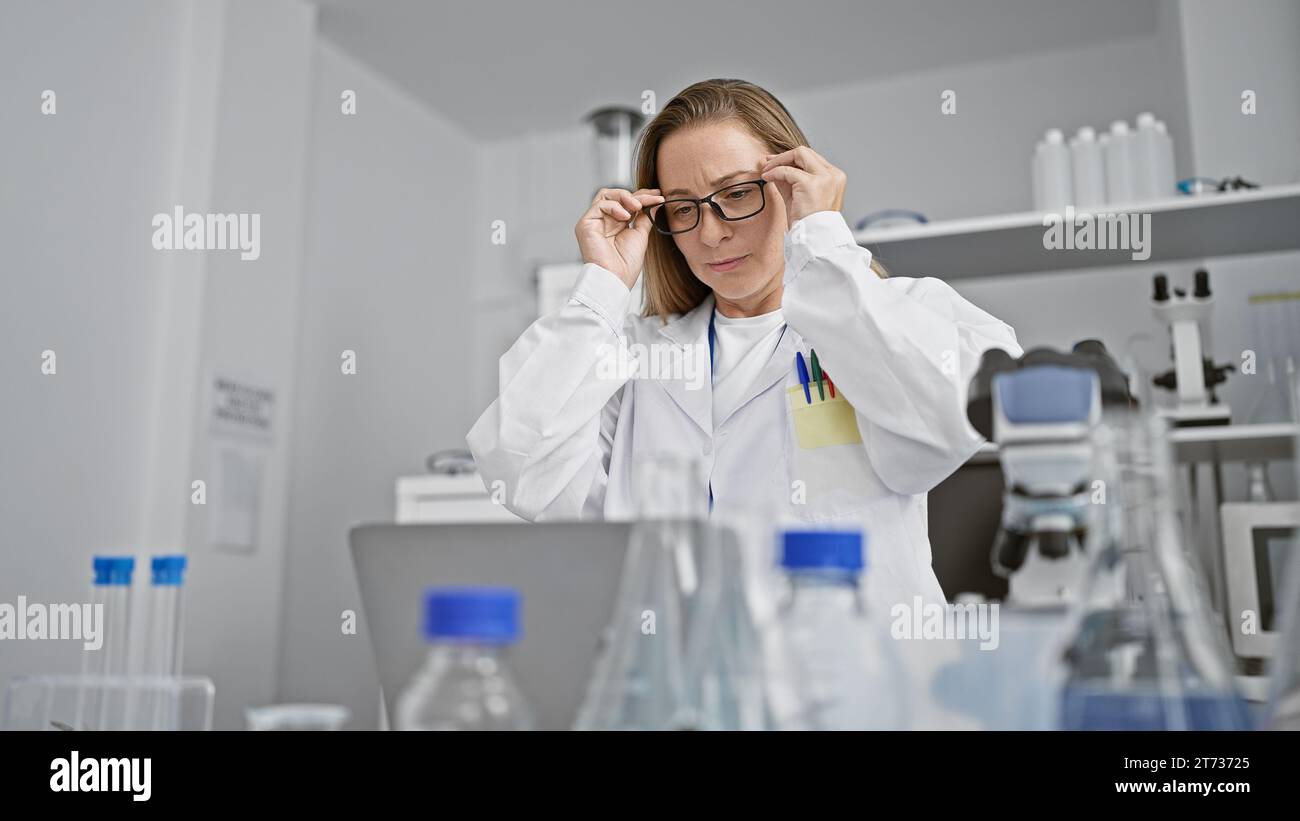 Serious young blonde woman scientist, engrossed with her work, dictates ...