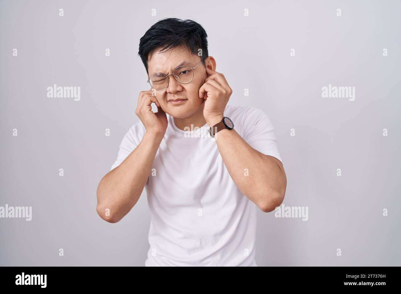 Young asian man standing over white background covering ears with ...
