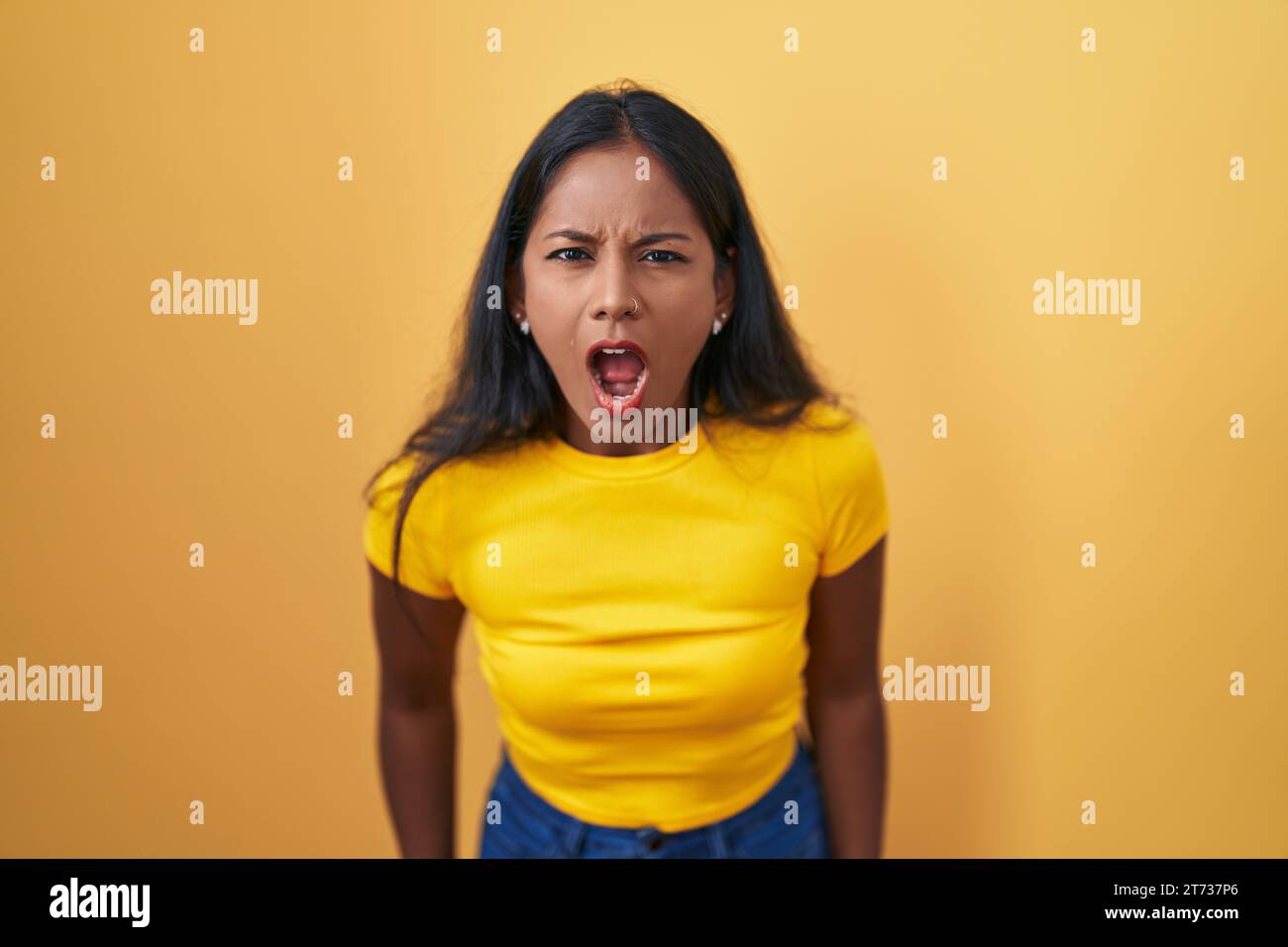 Young indian woman standing over yellow background angry and mad ...