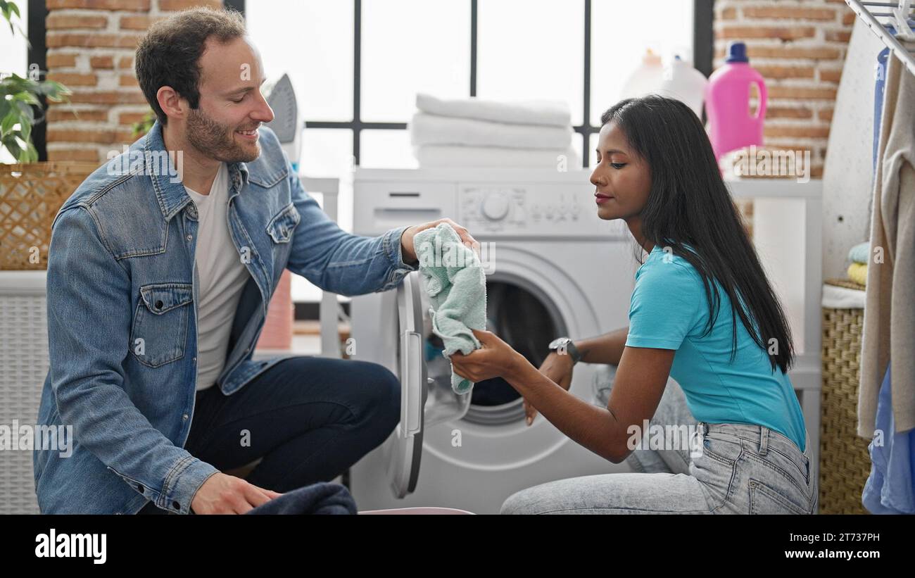 Beautiful couple smiling confident washing clothes at laundry room ...