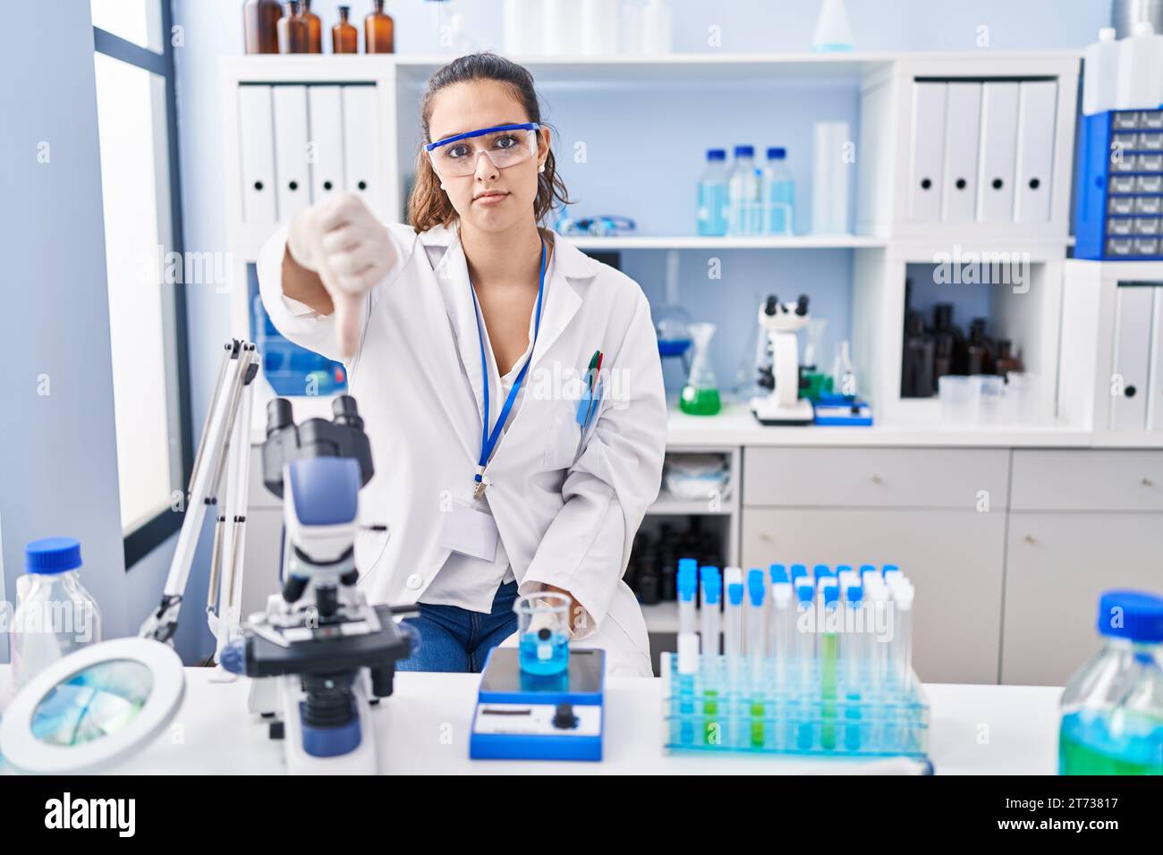 Young hispanic woman working at scientist laboratory looking unhappy ...