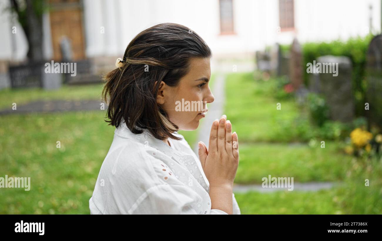 Beautiful young hispanic woman praying and mourning by tombstone at ...