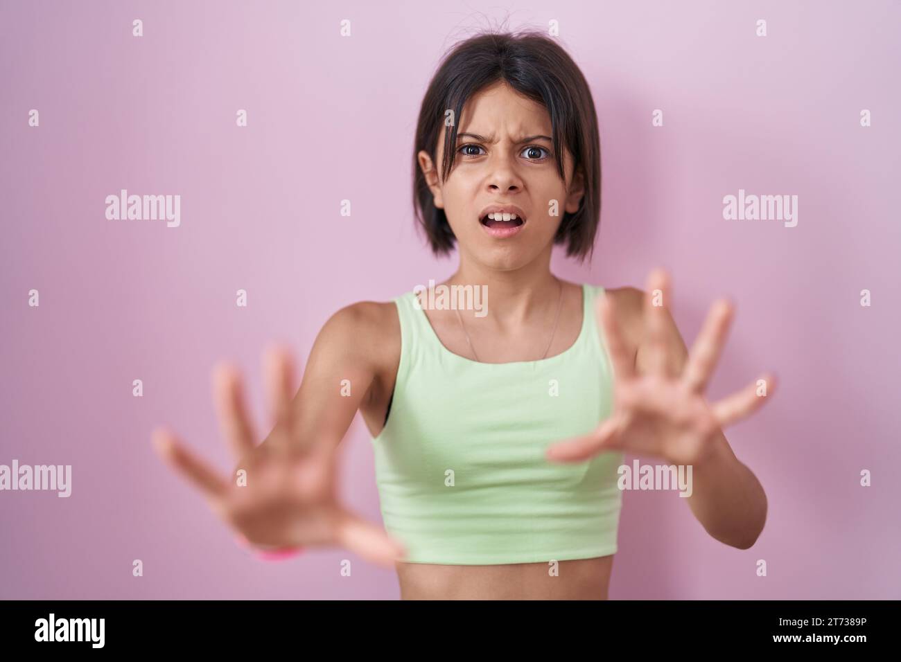 Young girl standing over pink background afraid and terrified with fear ...