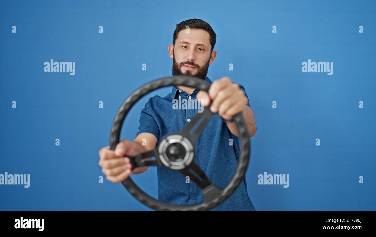 Young hispanic man using steering wheel as a driver over isolated blue ...
