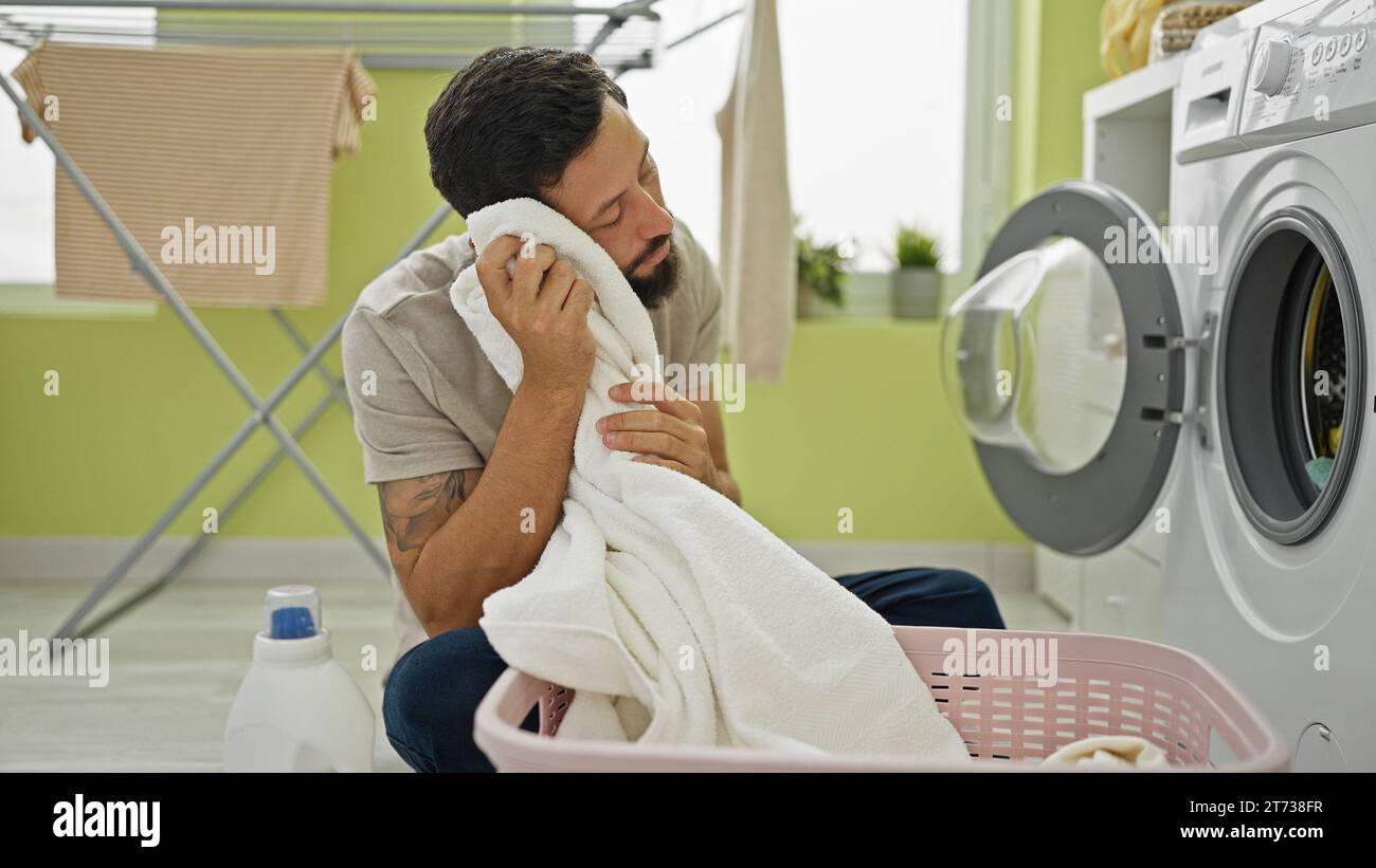 Young hispanic man washing clothes touching clean towel with face at ...