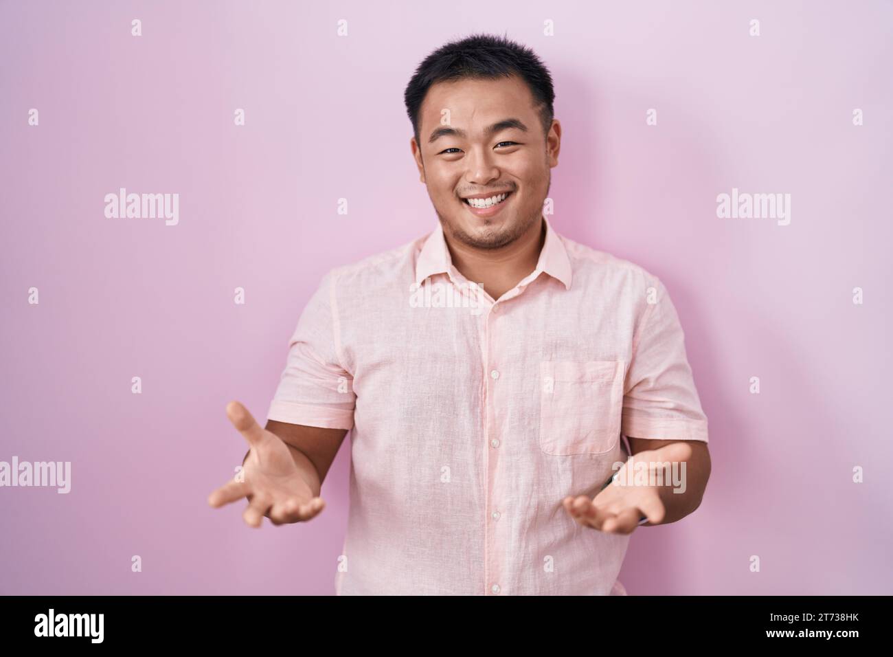 Chinese young man standing over pink background smiling cheerful with ...