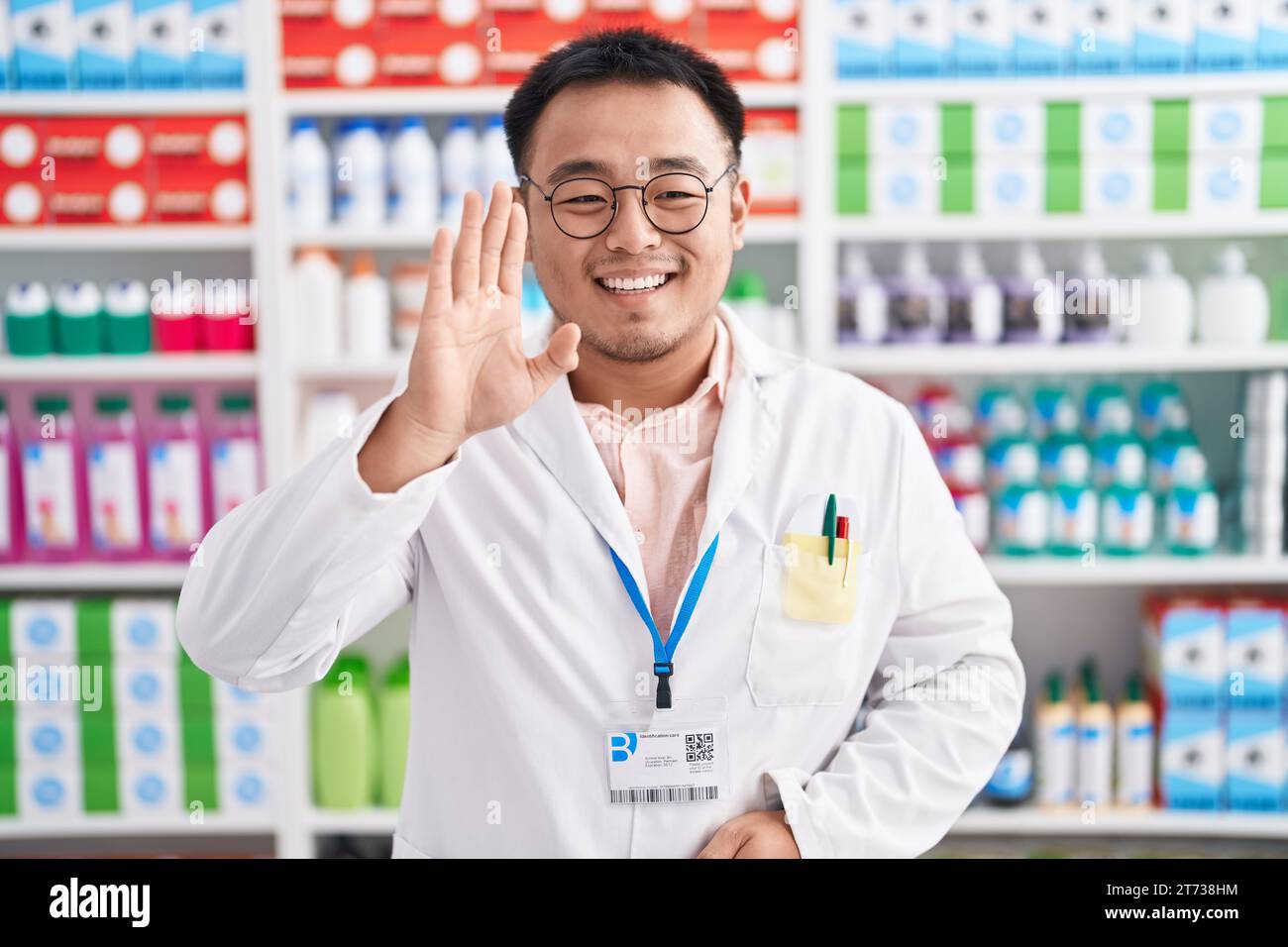 Chinese young man working at pharmacy drugstore waiving saying hello ...