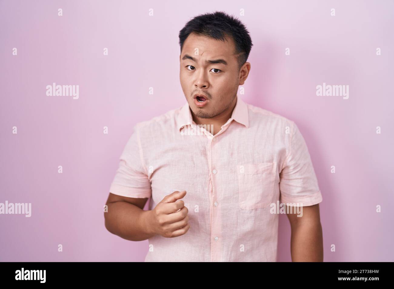 Chinese young man standing over pink background in shock face, looking ...