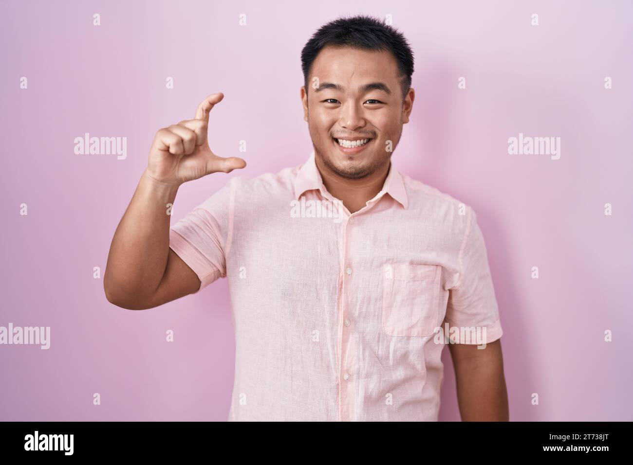 Chinese young man standing over pink background smiling and confident ...