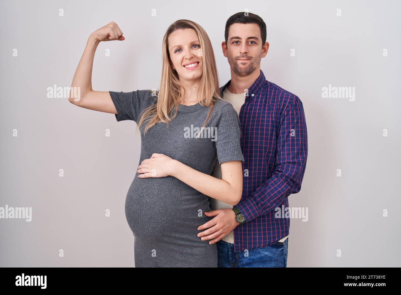 Young couple expecting a baby standing over white background strong ...
