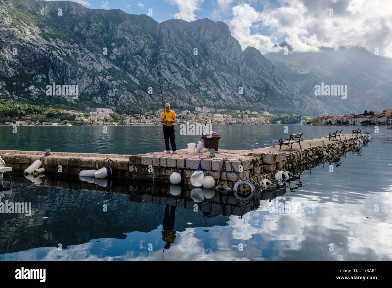 A local man fishing in the Bay of Kotor at Prčanj with Kotor in the ...