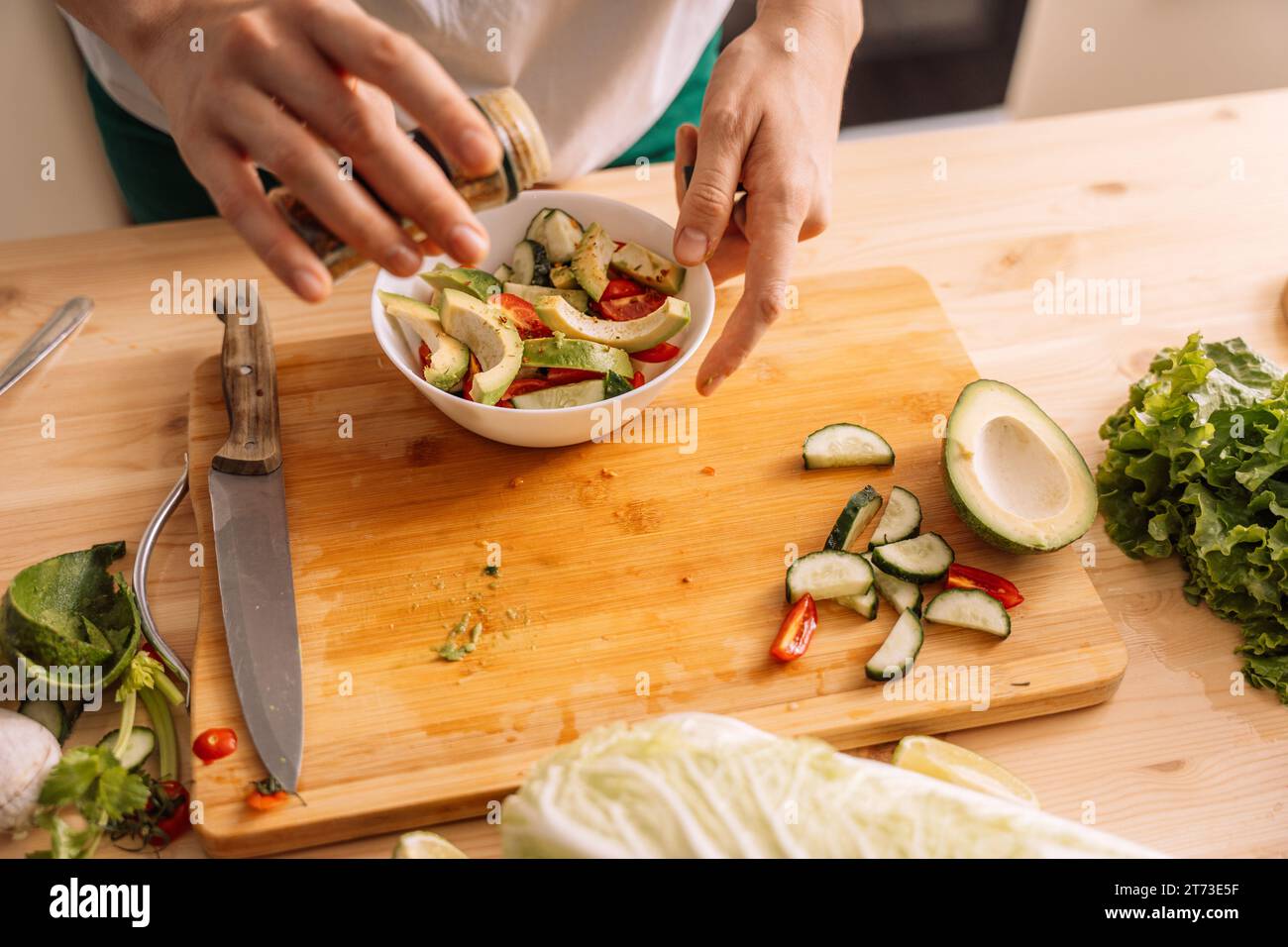 Lady sprinkles spices on vegetarian salad in a white plate on a wooden ...