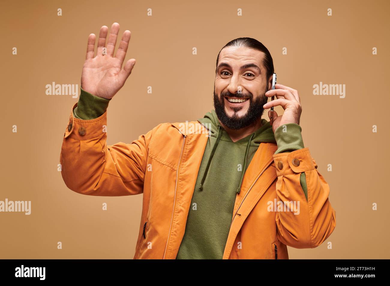 friendly middle eastern man with beard talking on smartphone on beige ...