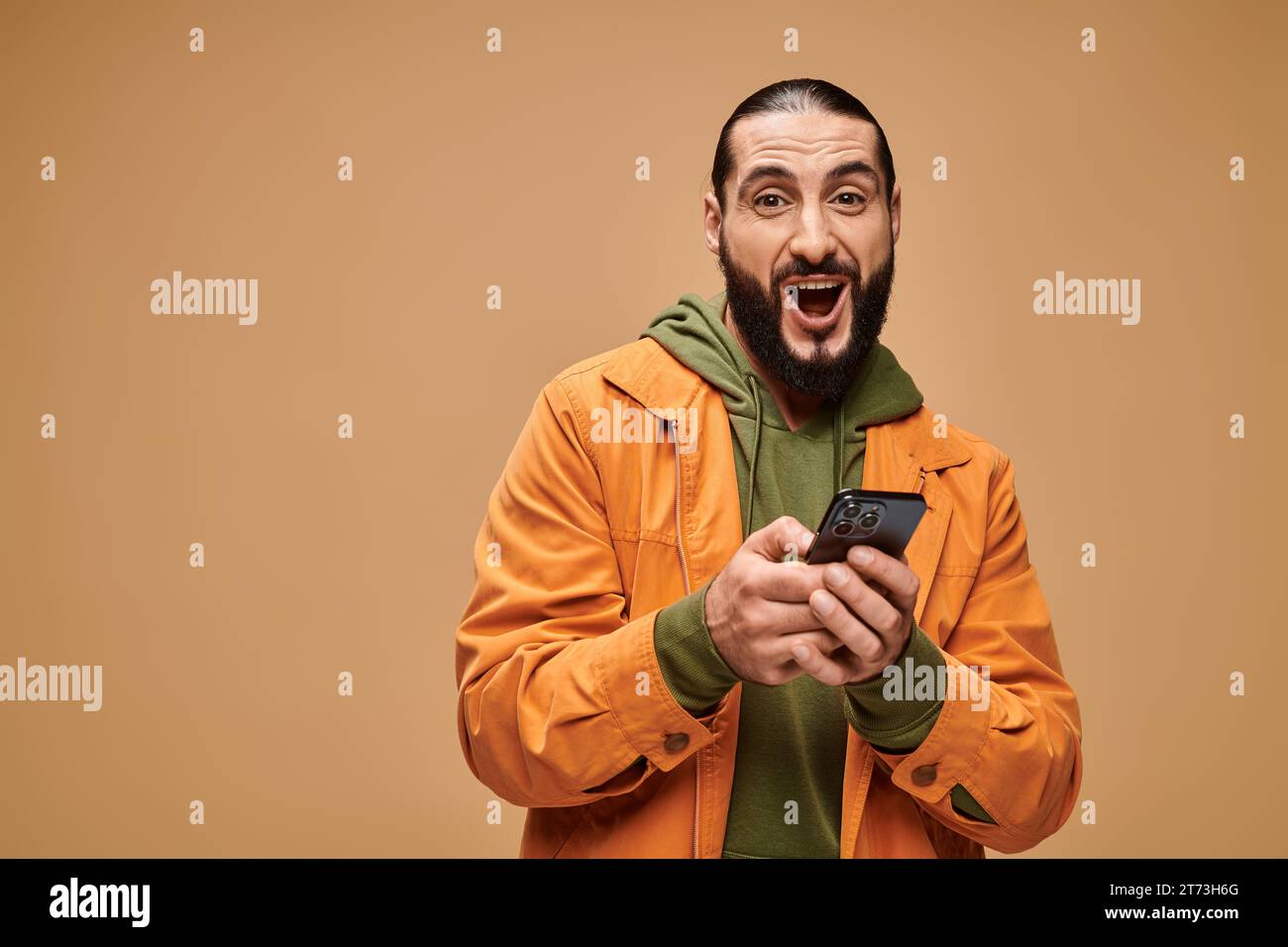 happy middle eastern man with beard using smartphone on beige ...