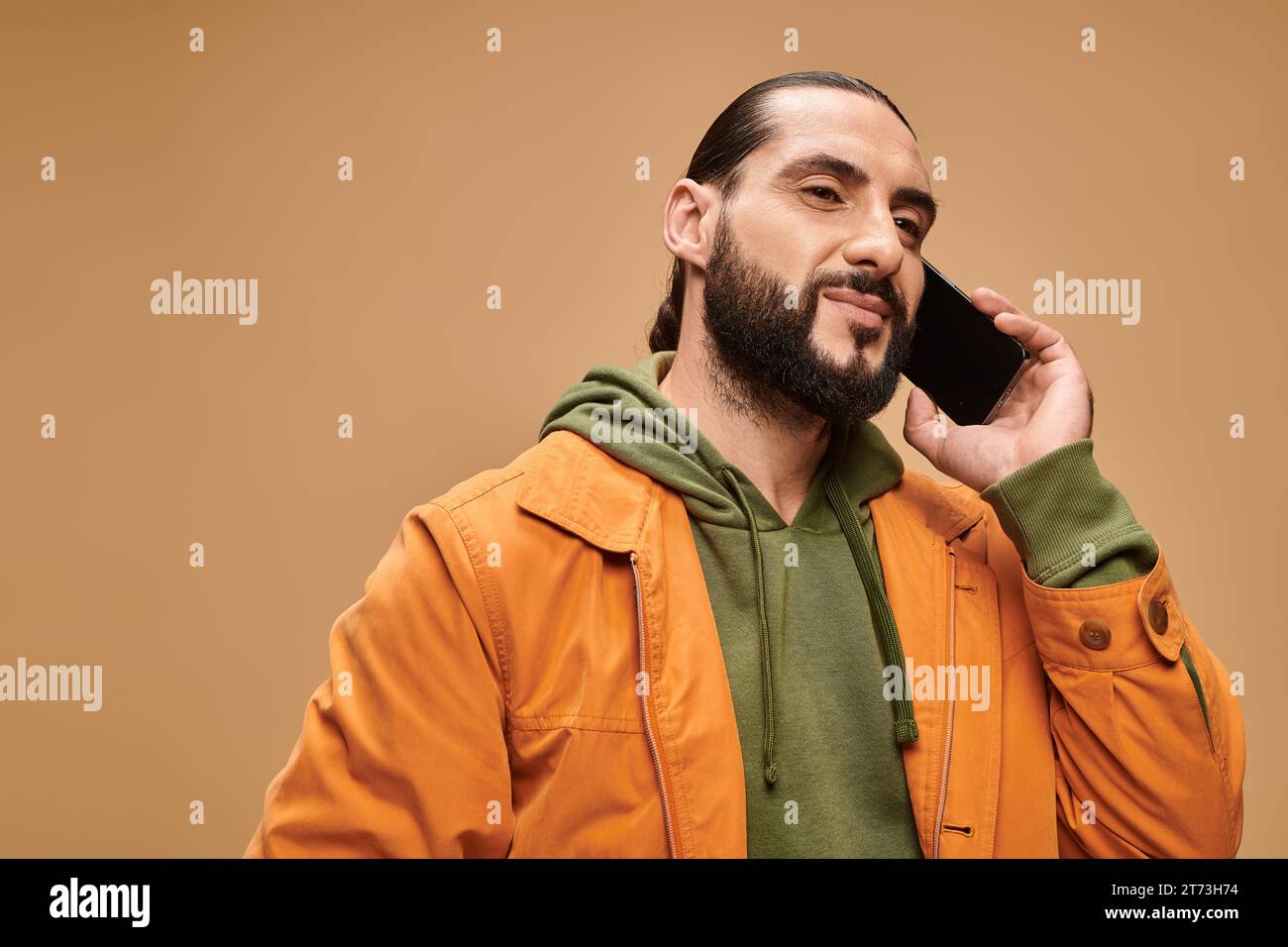 handsome middle eastern man with beard talking on smartphone on beige ...