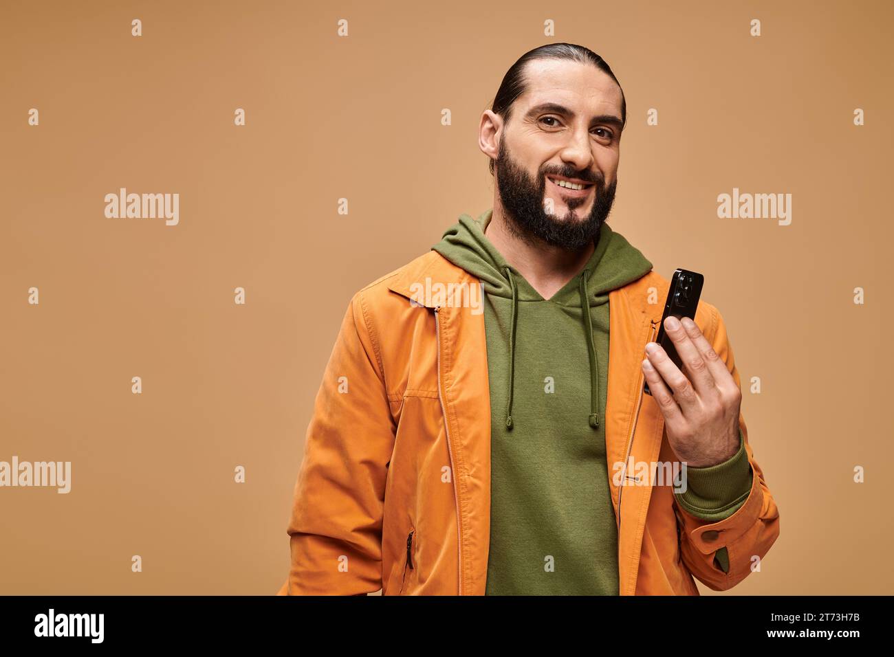 happy middle eastern man with beard holding smartphone on beige ...