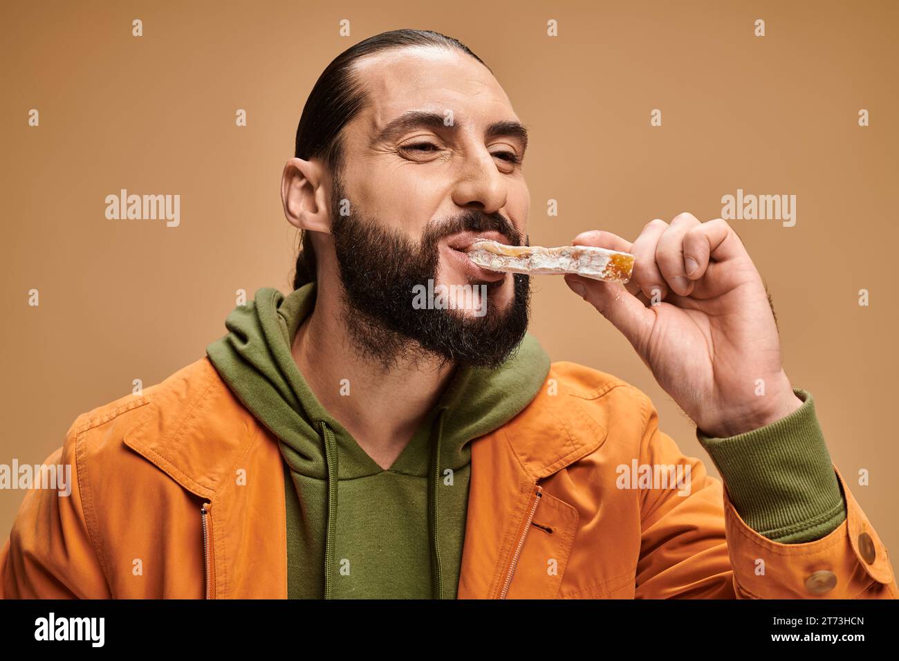 cheerful and bearded arabic man eating delicious cevizli sucuk on beige ...