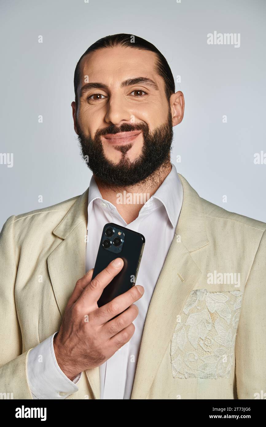 happy bearded arabic man in stylish formal wear holding smartphone on ...
