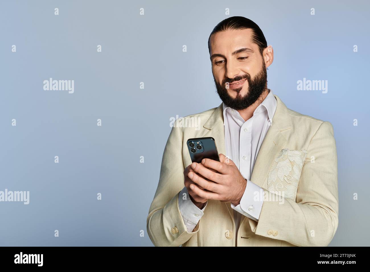 happy bearded arabic man in white formal wear using smartphone on grey ...