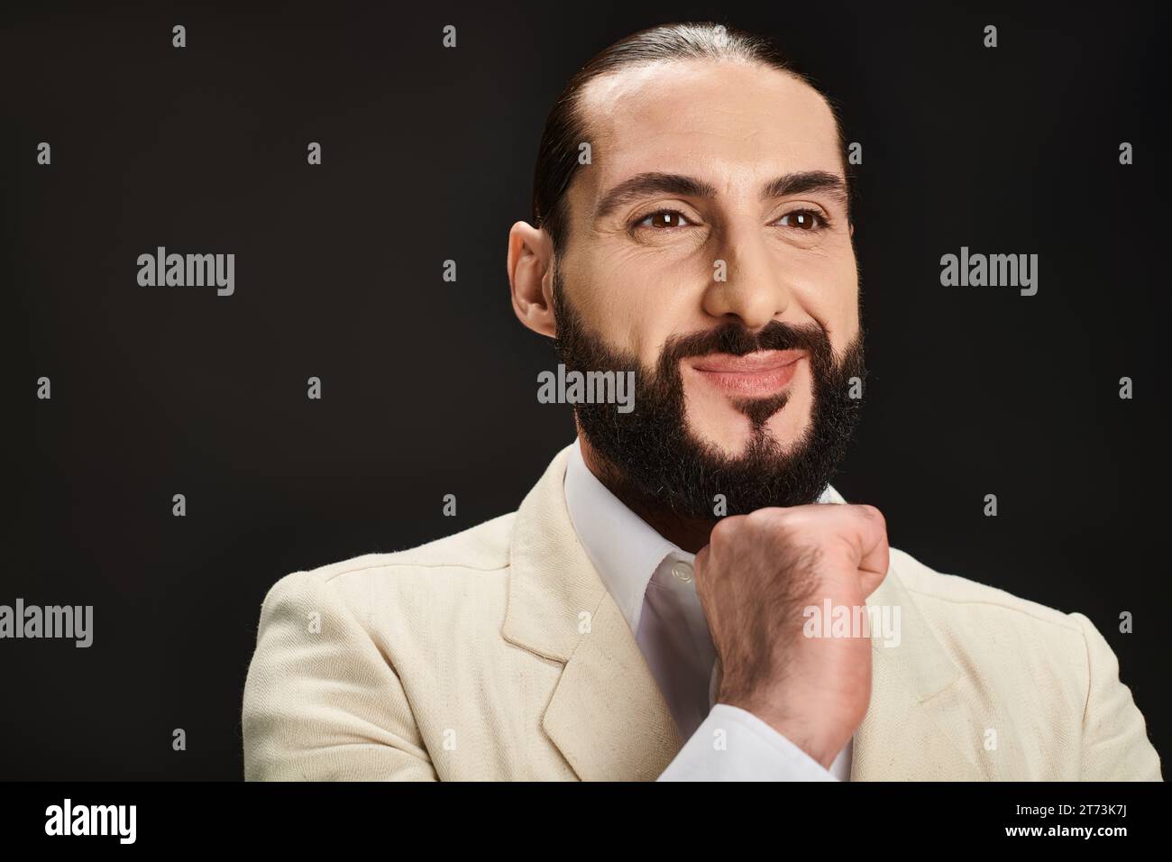 positive and bearded arabic man in white shirt and blazer looking at ...