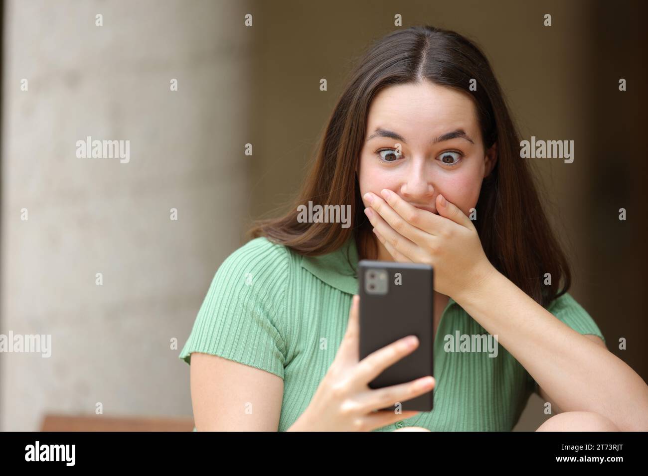 Front view portrait of a surprised woman checking cell phone news in the street Stock Photo - Alamy