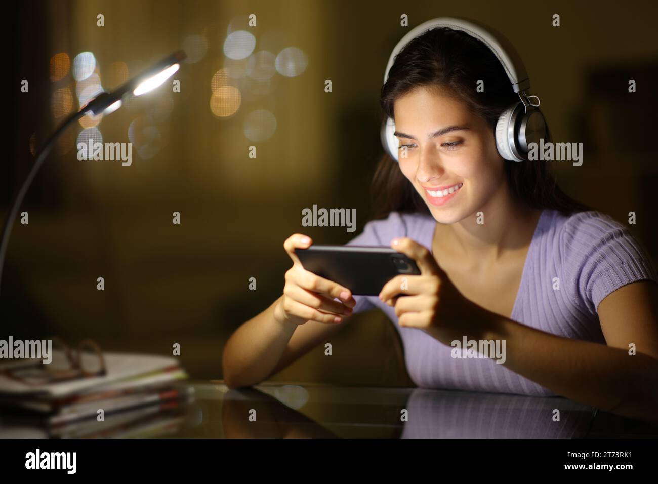 Happy woman wearing headphone in the night watching videos on phone at ...