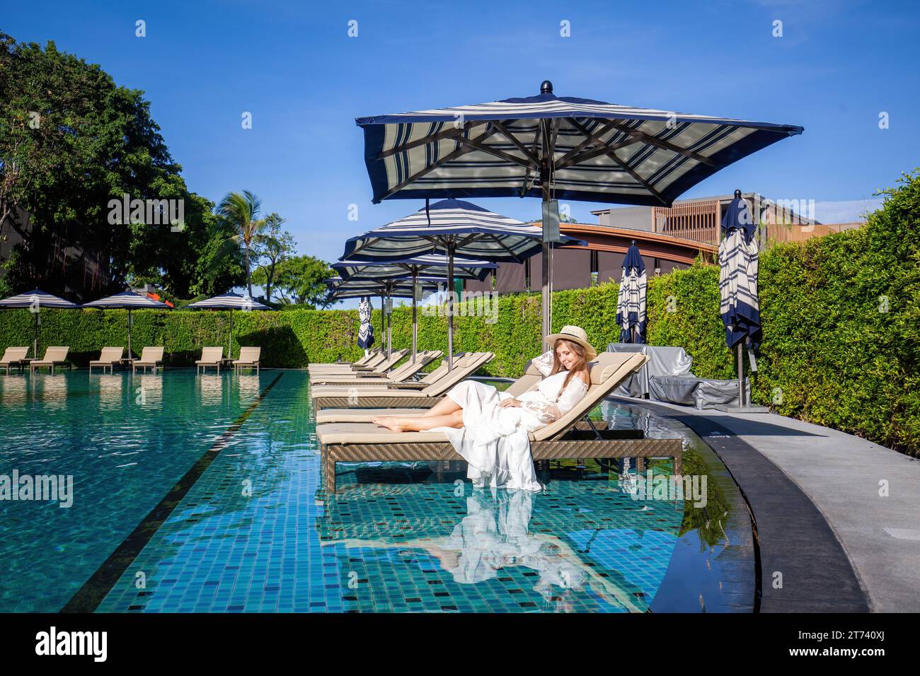 Woman in elegant white dress by the pool at a tropical Thai resort ...