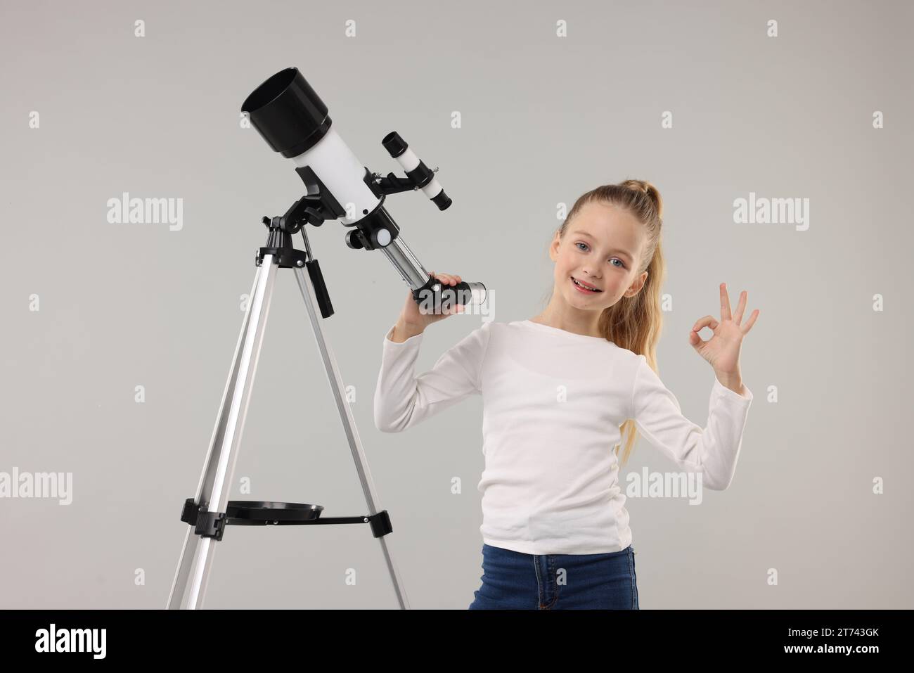 Happy little girl with telescope showing ok gesture on light grey ...