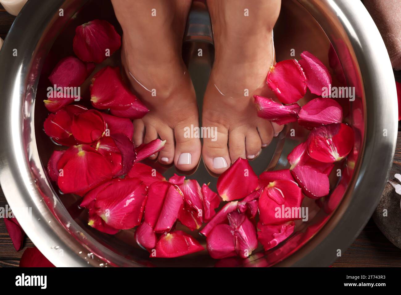 Woman soaking her feet in bowl with water and red rose petals, top view ...