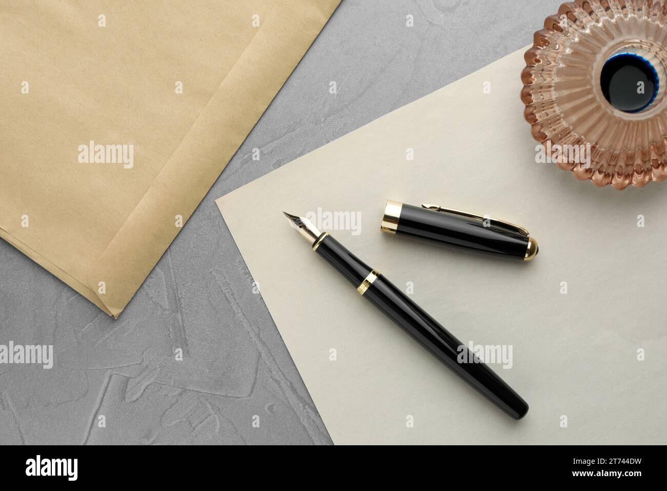 Stylish fountain pen, inkwell, envelope and paper on grey textured ...