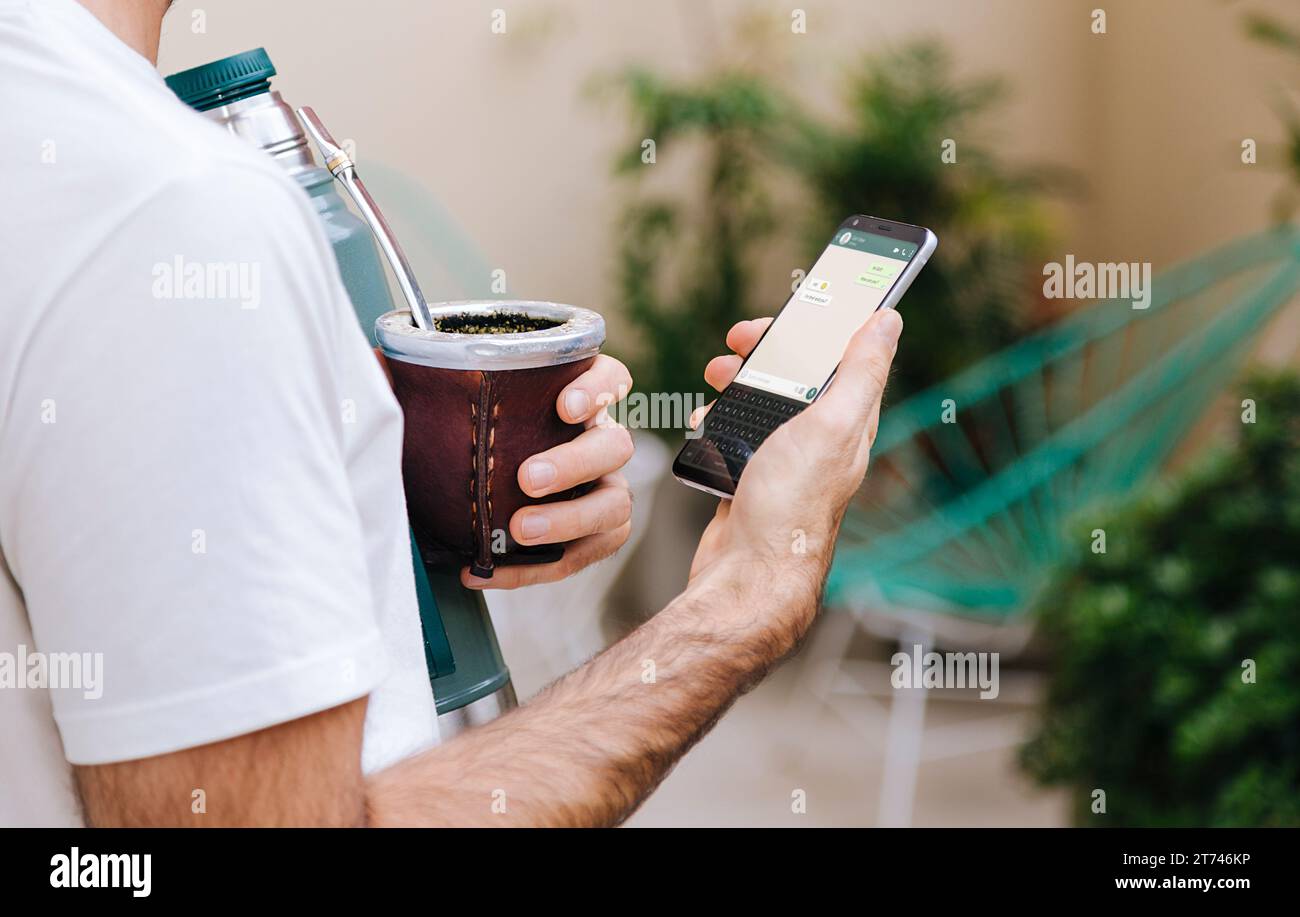 Man with a gourd Mate and thermos holding a cell phone in his hand with ...